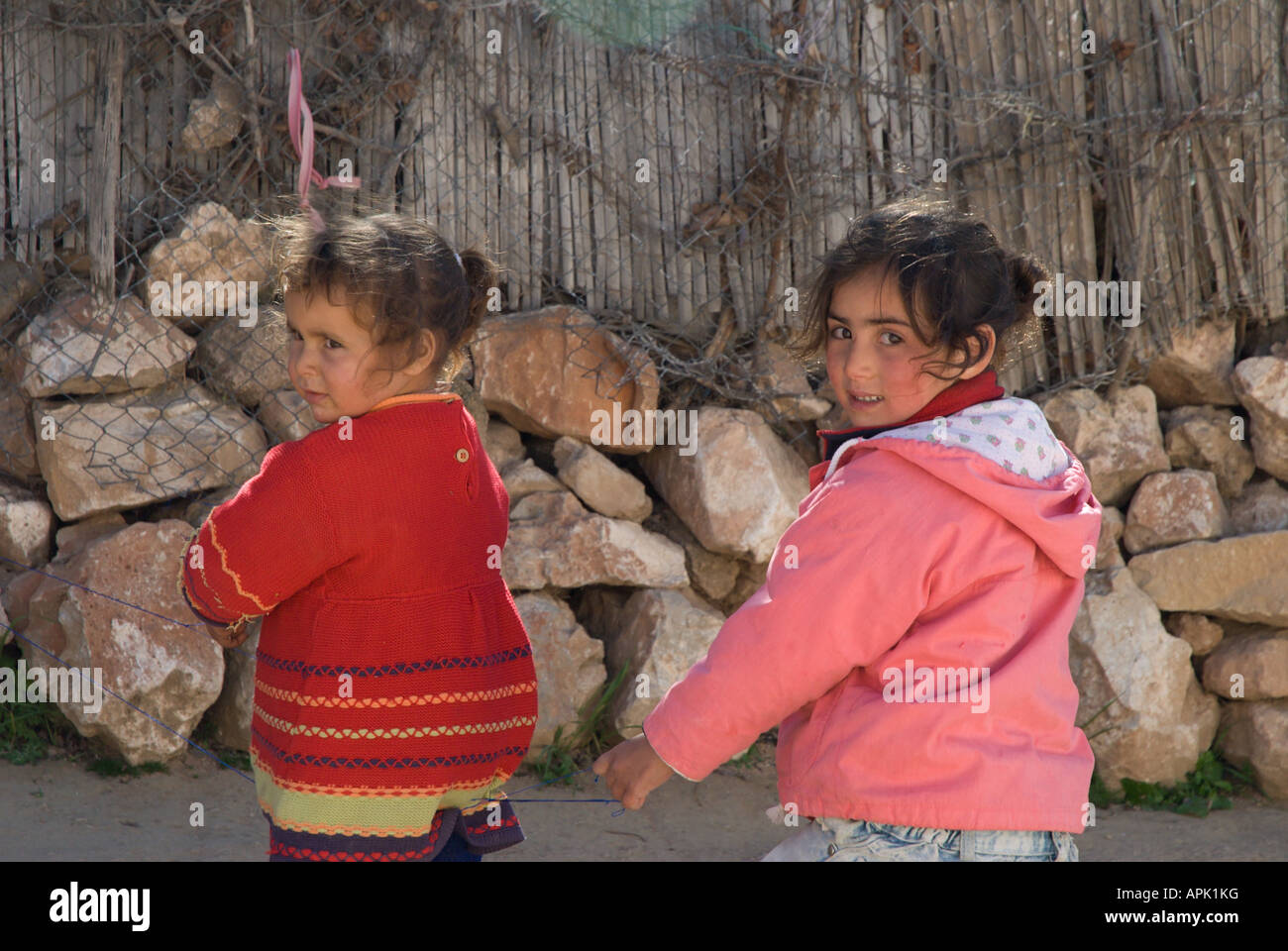 Two Moroccan girls in red and pink look over their shoulders while ...