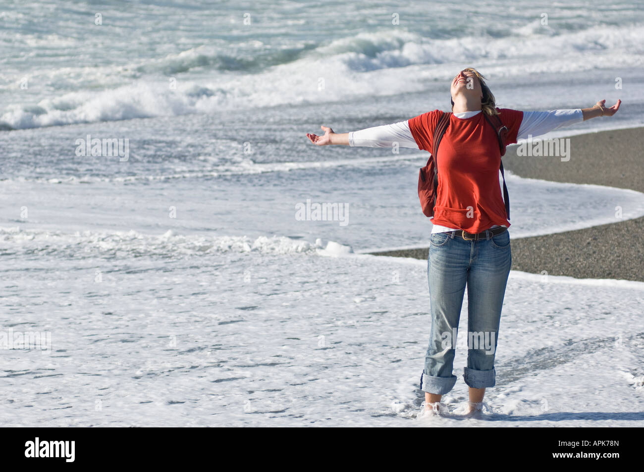 Happy female wading through water of Tasman sea on empty west coast ...