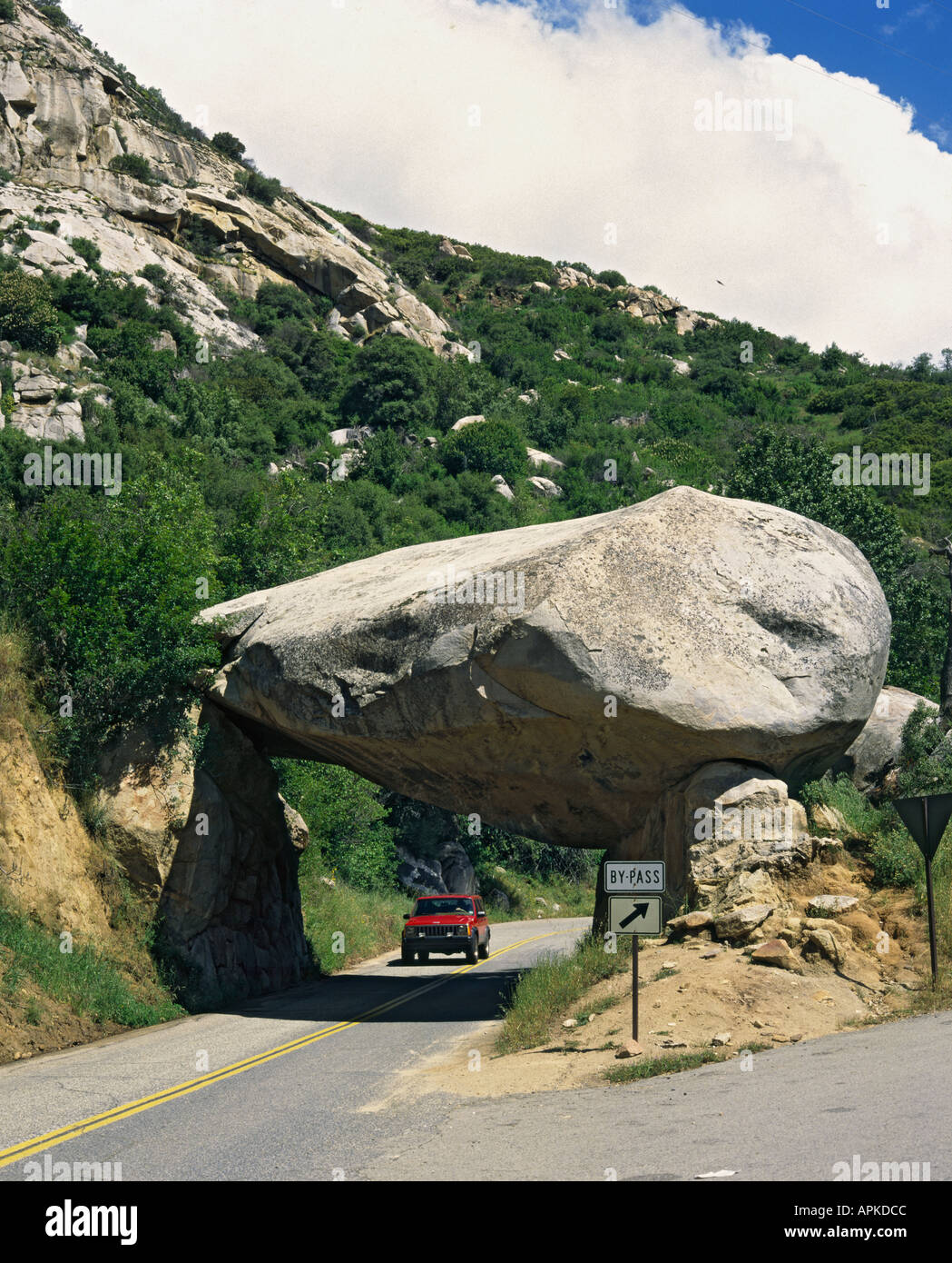 A red car about to pass under a huge rock balanced at either end across ...