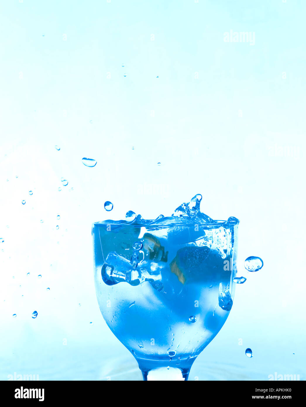 Cube of ice splashes into glass of water Stock Photo - Alamy
