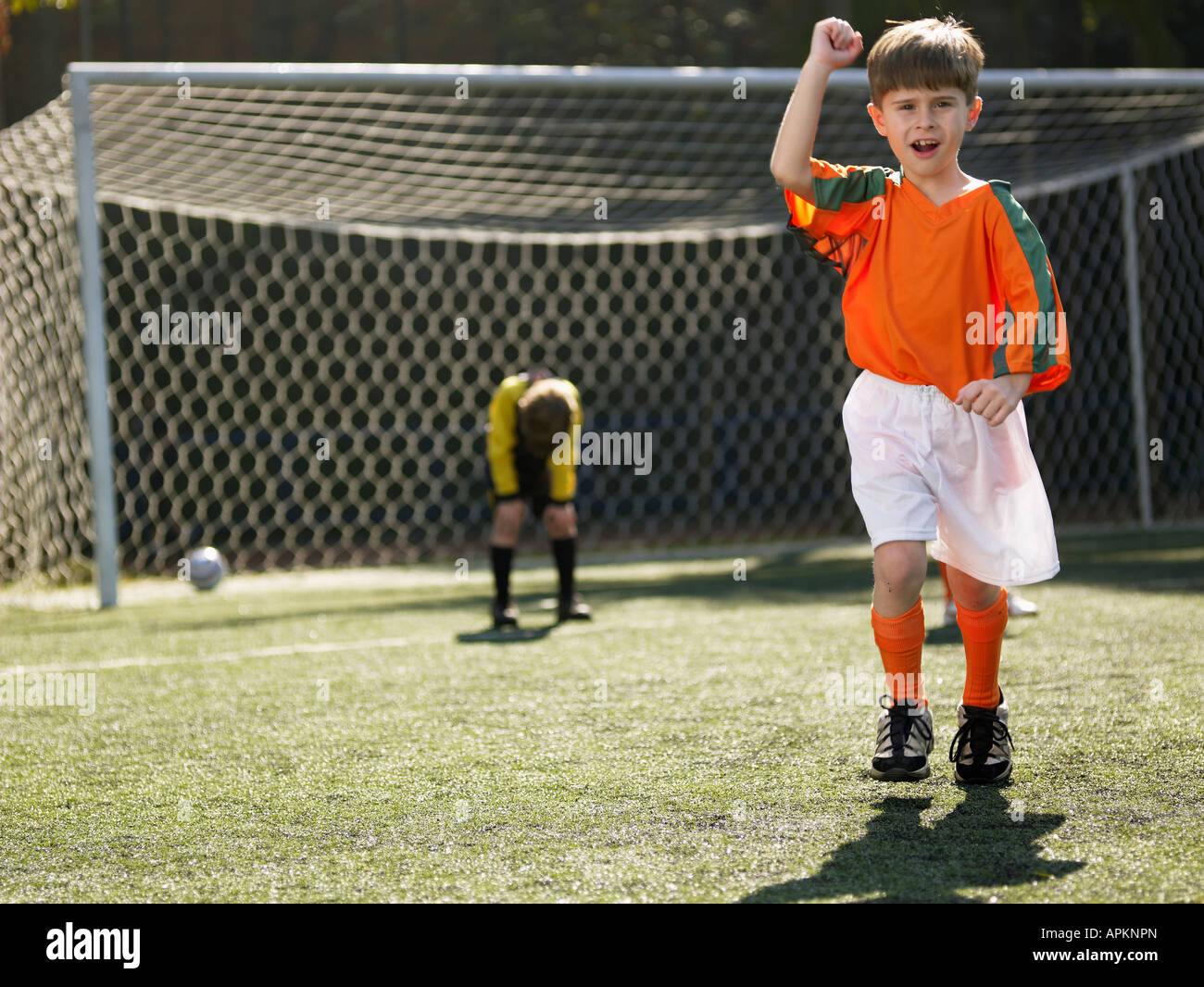 Boy in soccer uniform celebrating, defeated goalkeeper in background ...
