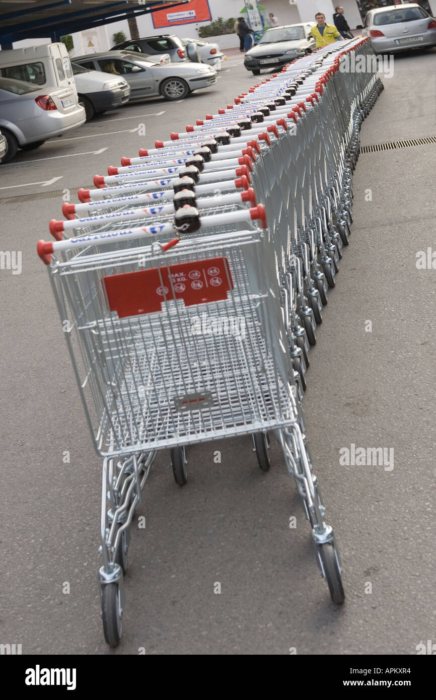 Man pulling long row of shopping trolleys in supermarket parking area ...
