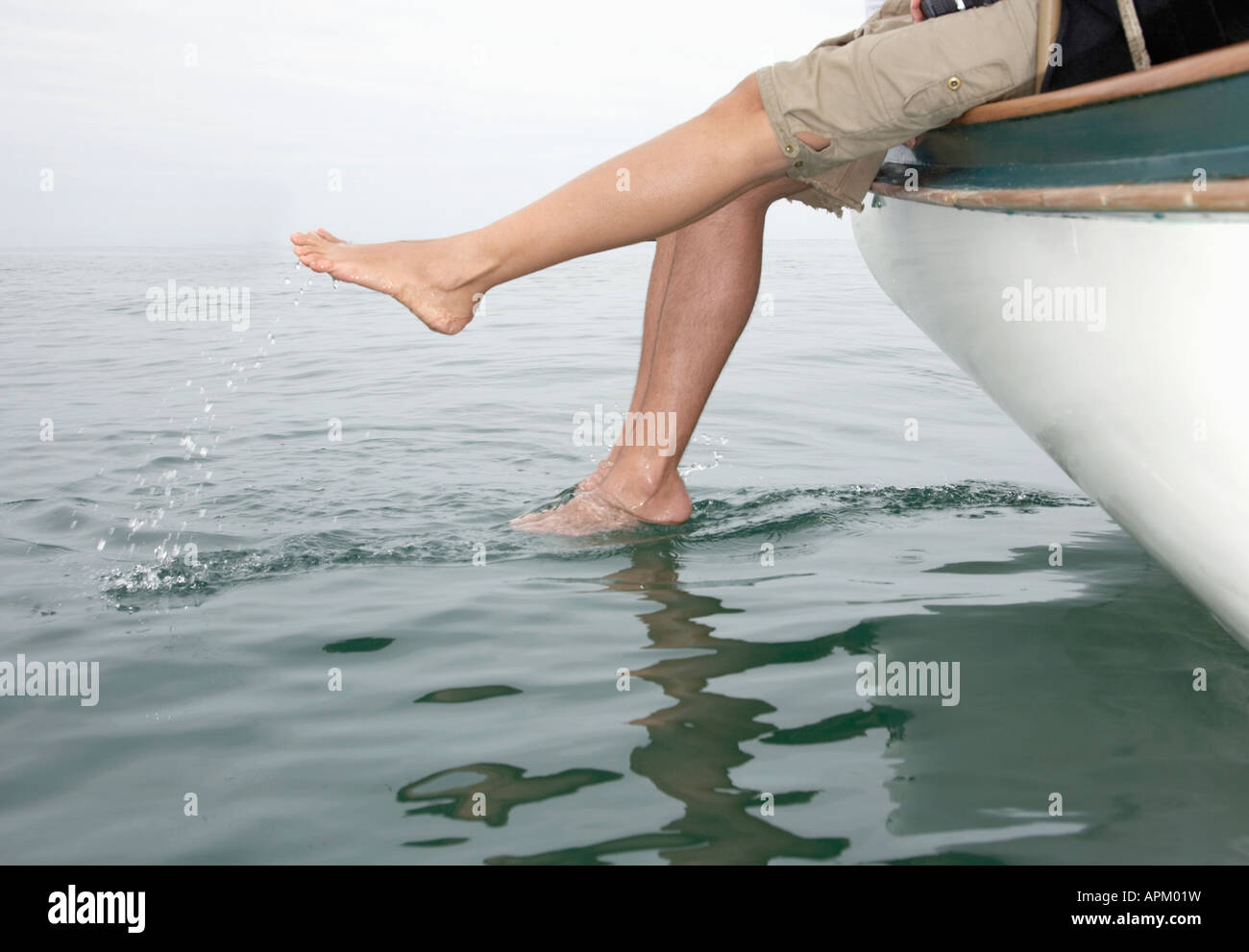 Couple sitting on edge of boat, dipping feet in water (low angle view ...