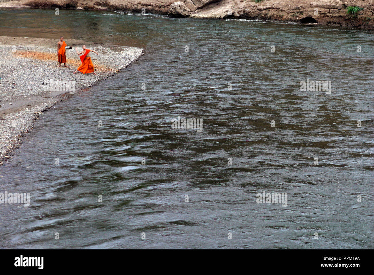 two monks in orange robes compete to throw stones into the river Stock ...