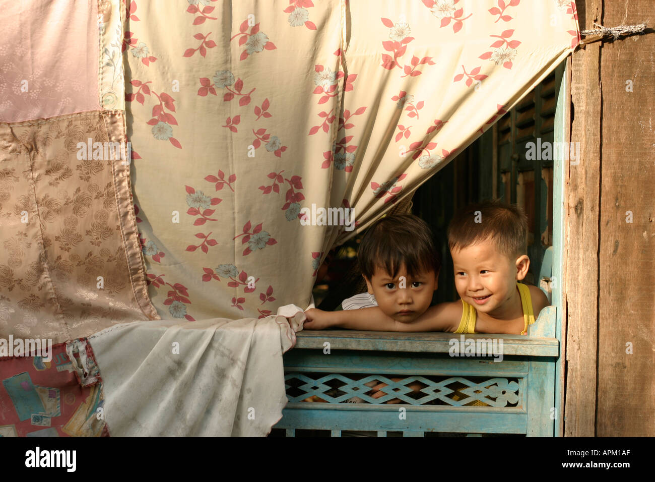 Two boys looking out from a curtained window Stock Photo - Alamy