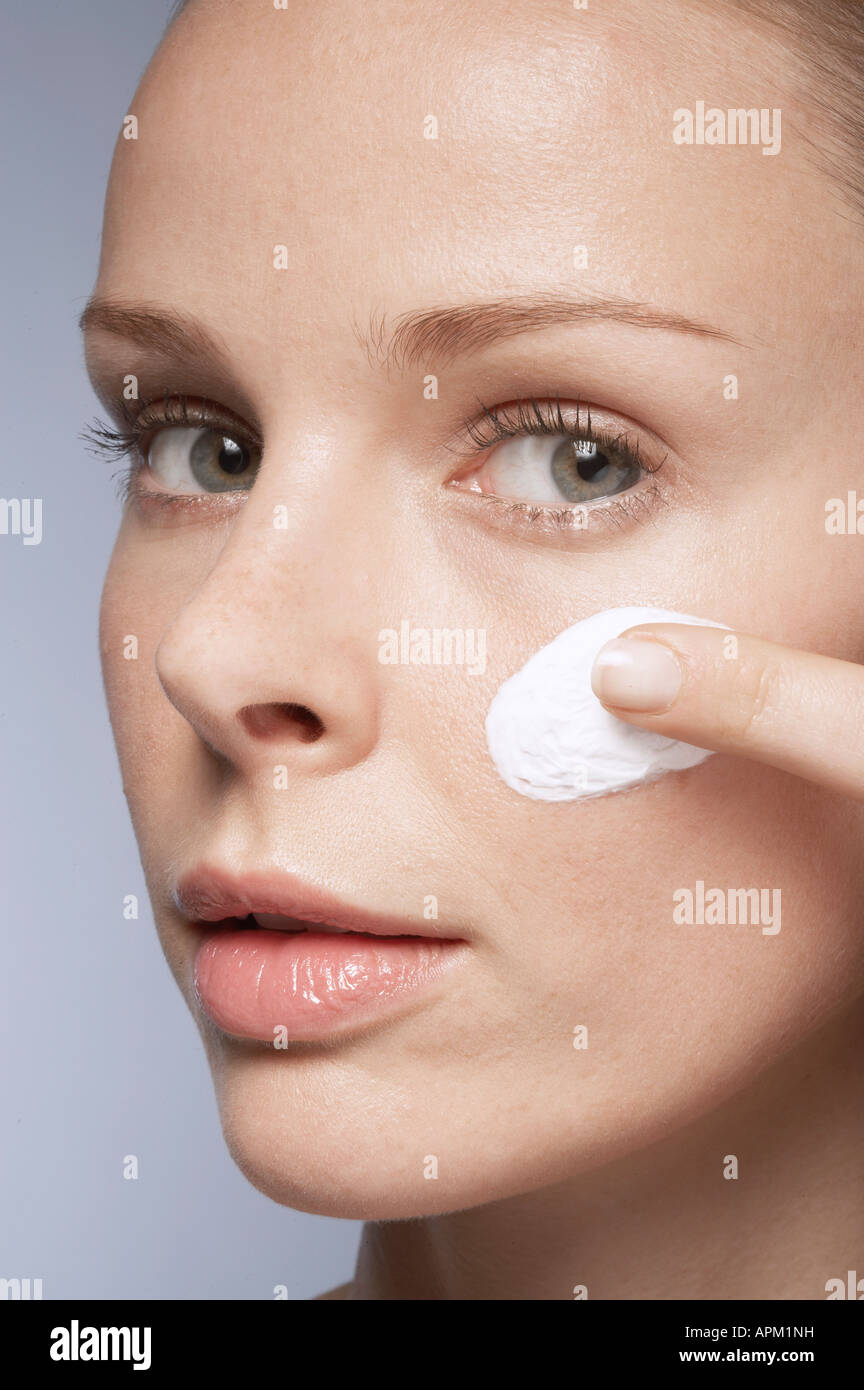 Young woman applying moisturizer on face Stock Photo - Alamy
