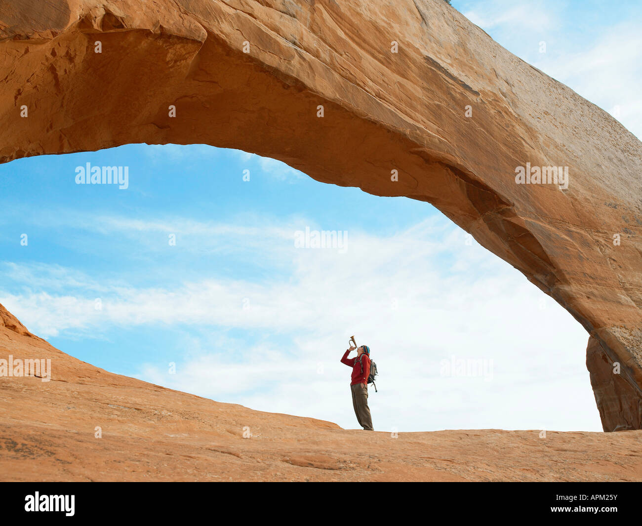 Young man playing bugle under arched rock Stock Photo - Alamy