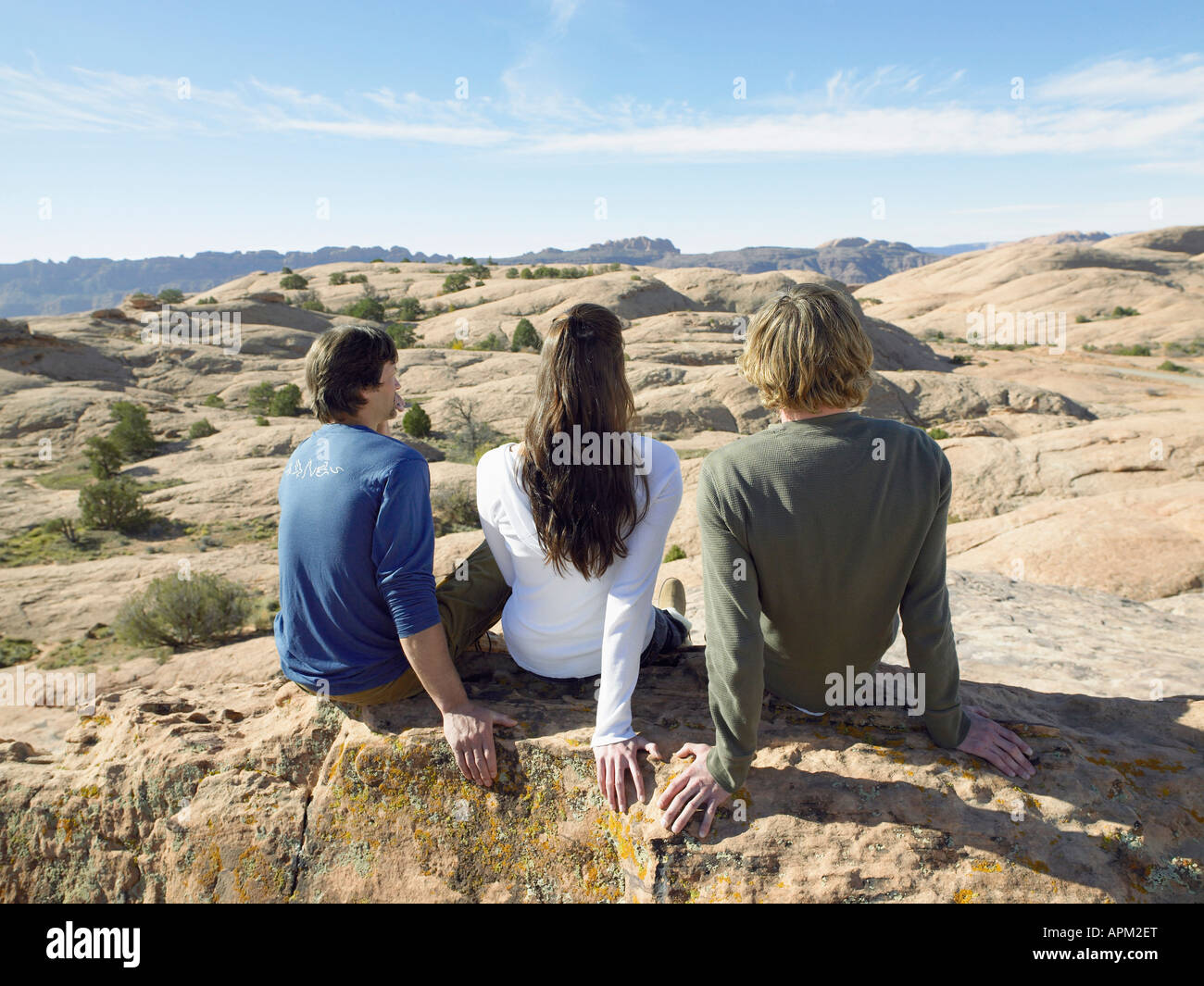 Three friends sitting on rocks, rear view Stock Photo - Alamy