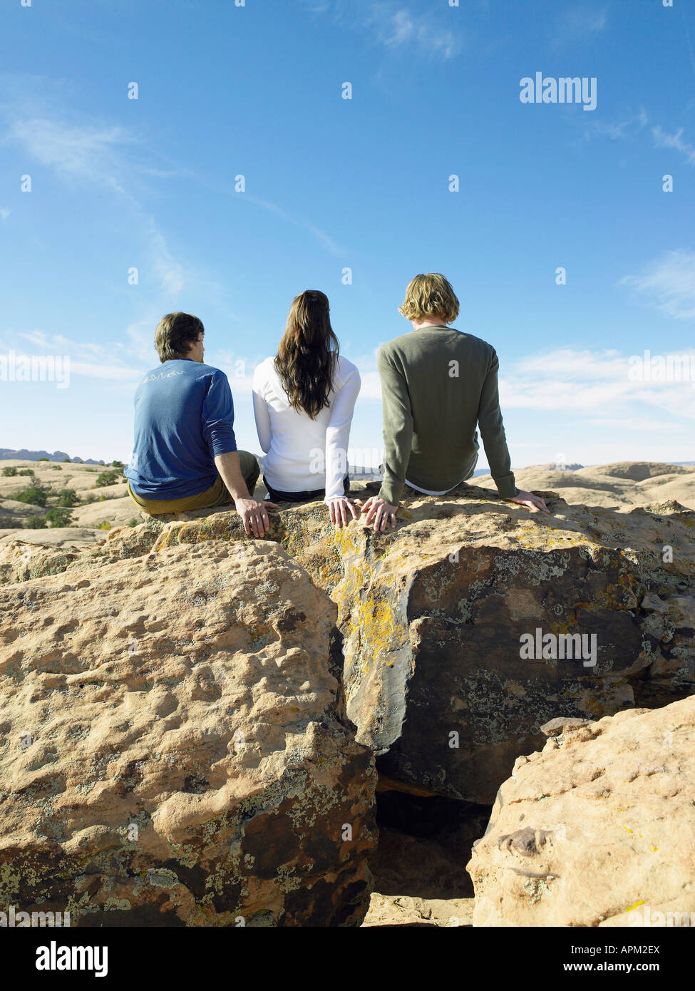 Three friends sitting on rocks, rear view Stock Photo - Alamy