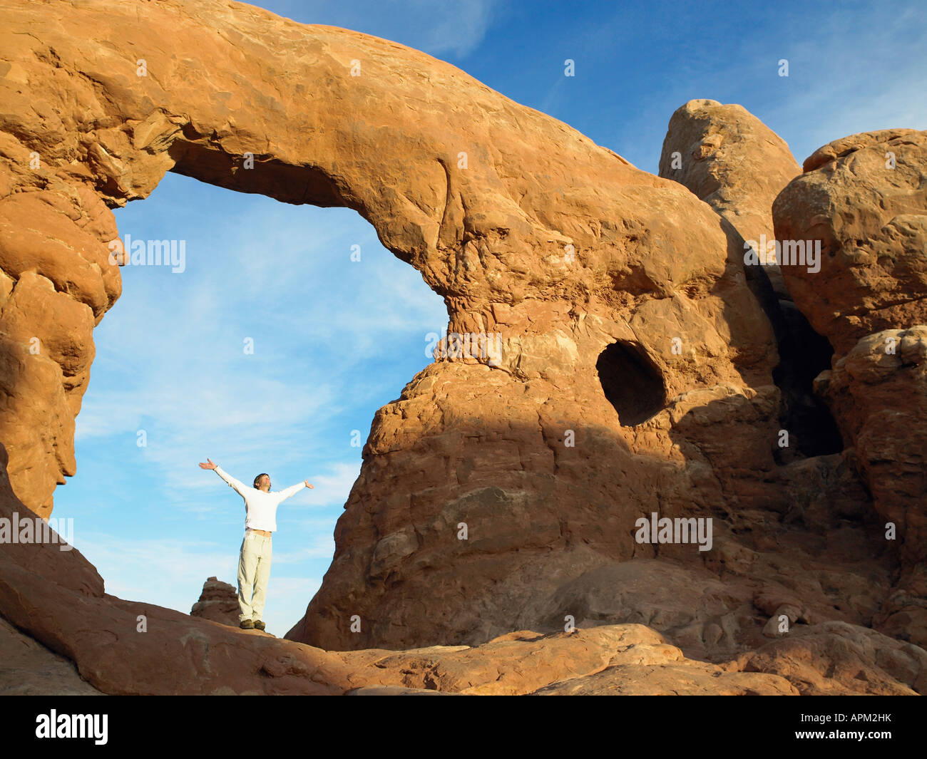 Man standing under arched rock with arms raised Stock Photo - Alamy