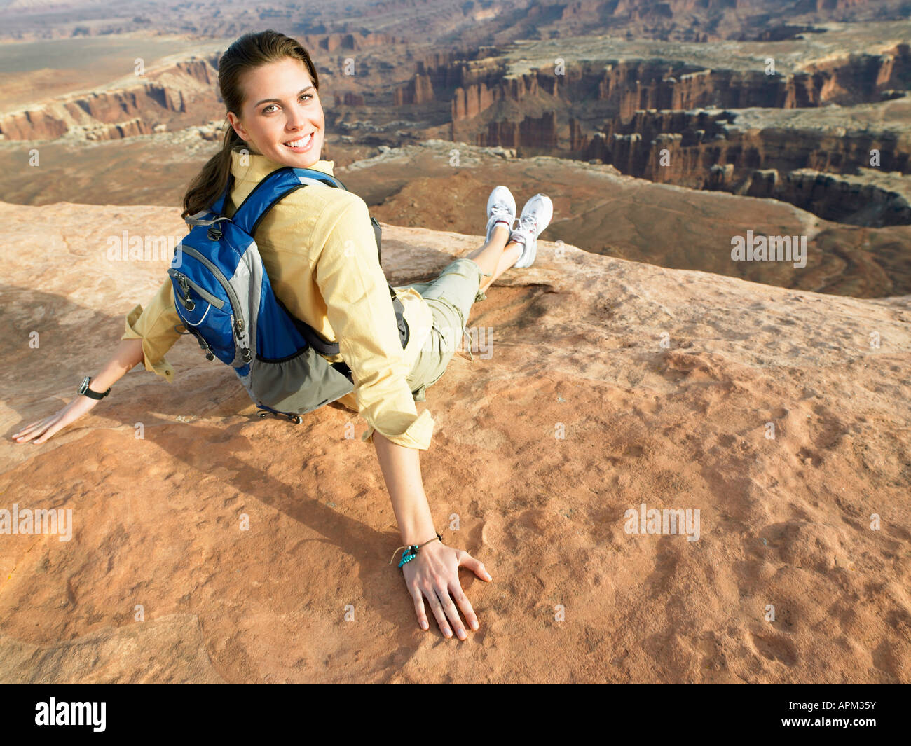 Young woman with backpack sitting on cliff, rear view Stock Photo - Alamy