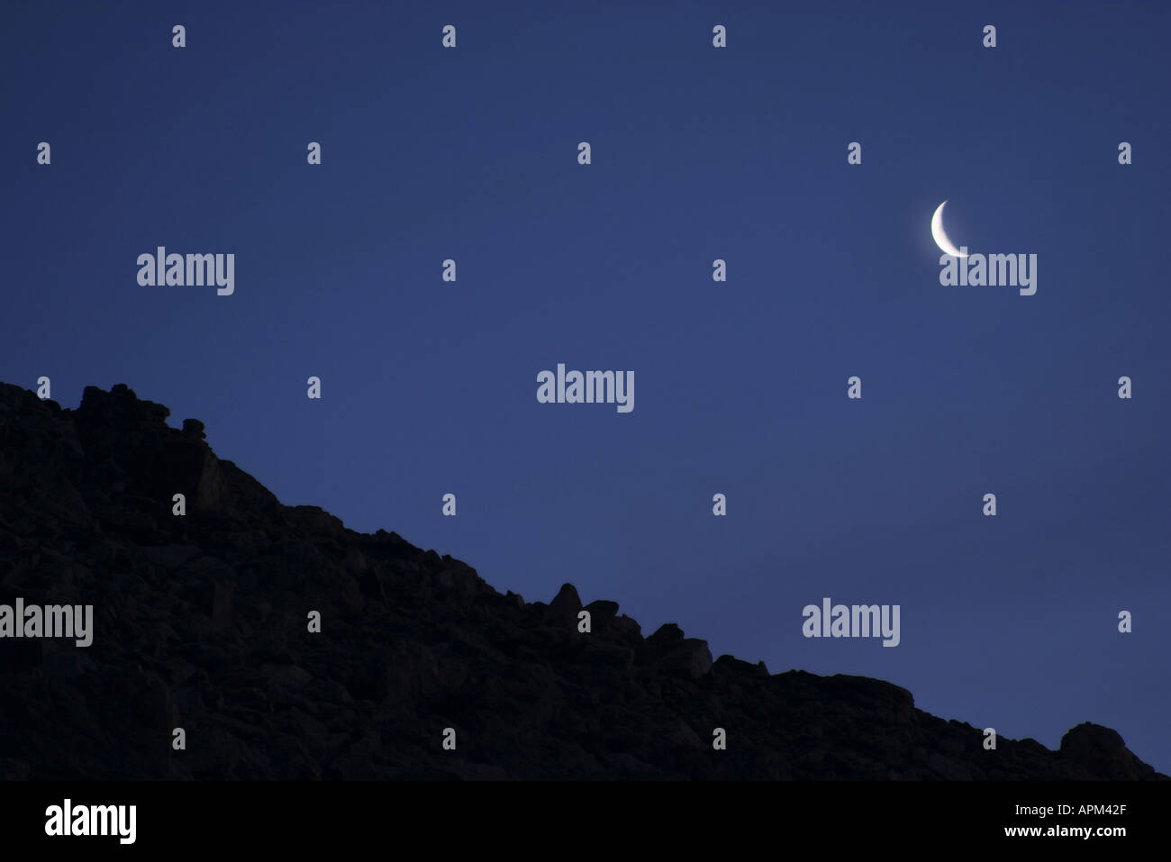 Crescent moon above silhouetted ridge line in clear night sky Stock ...