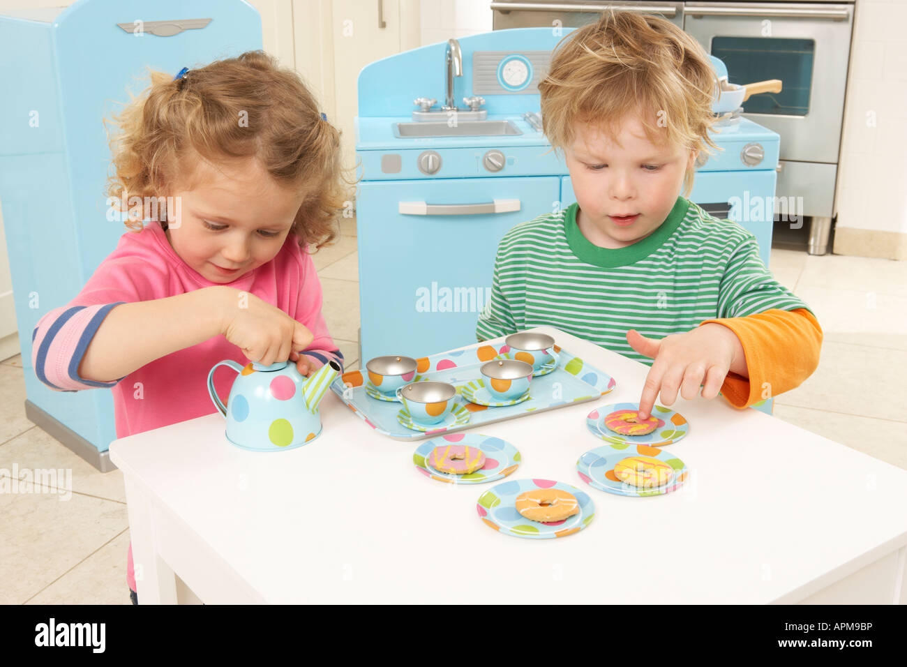 a boy and a girl play in a kitchen with a toy spotty tea set Stock ...