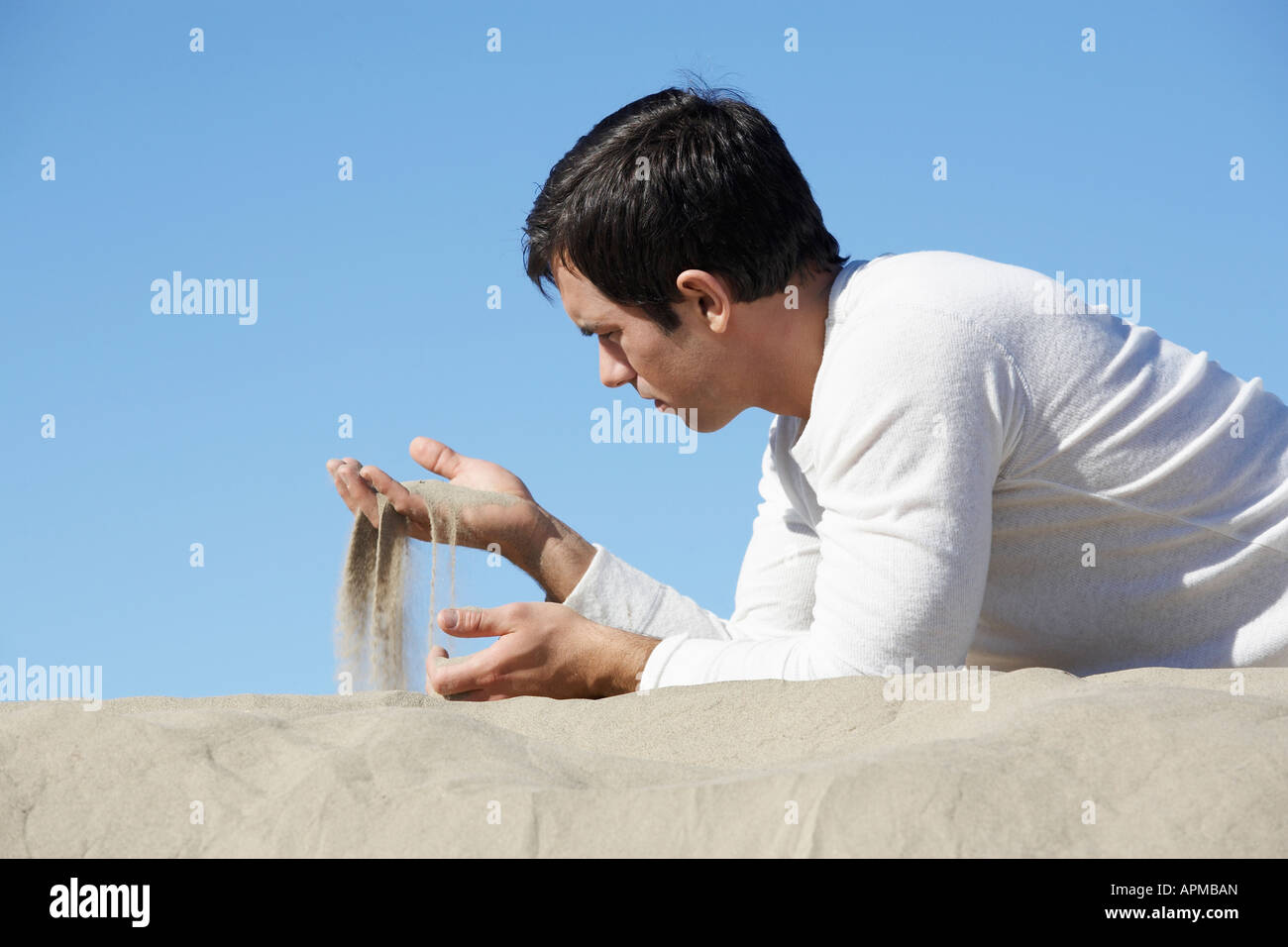 Man lying on front and sifting sand through hand Stock Photo - Alamy