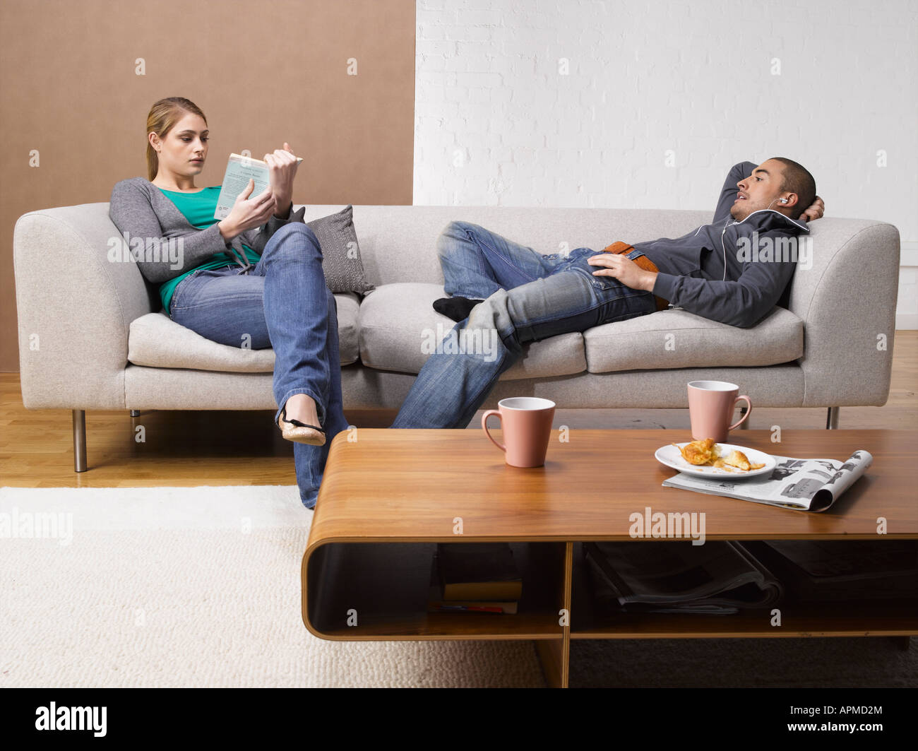 Young woman reading book and young man listening to MP3 player on sofa ...