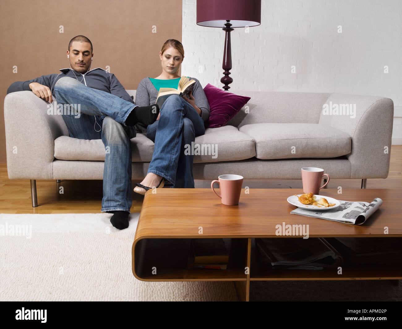 Young woman reading book and young man listening to MP3 player on sofa ...