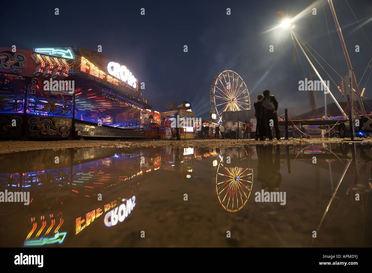 Fairground rides reflected in standing water at dusk Hull fair Kingston ...