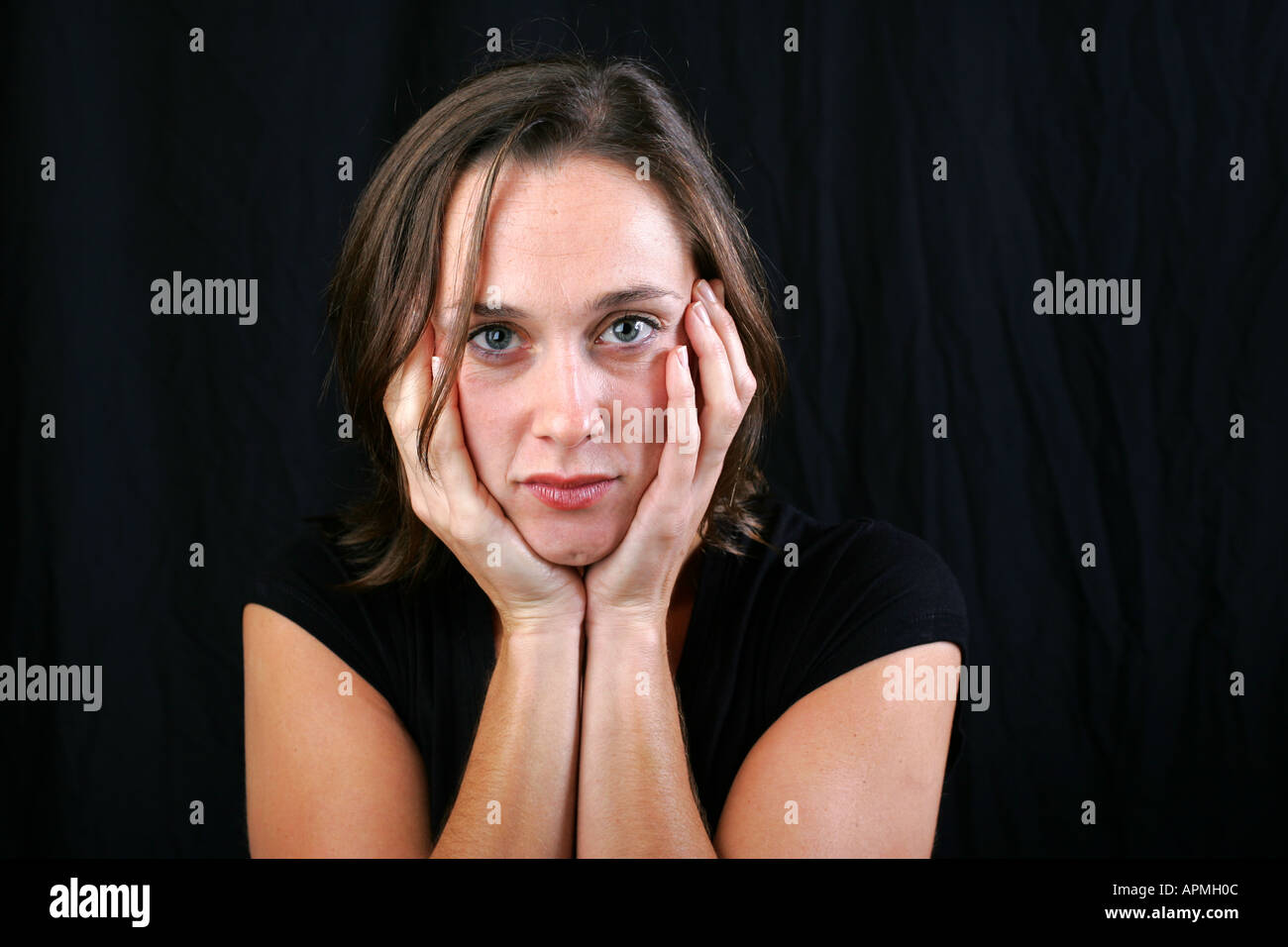 Young brunette woman with faint smile holds her head in hands looking ...