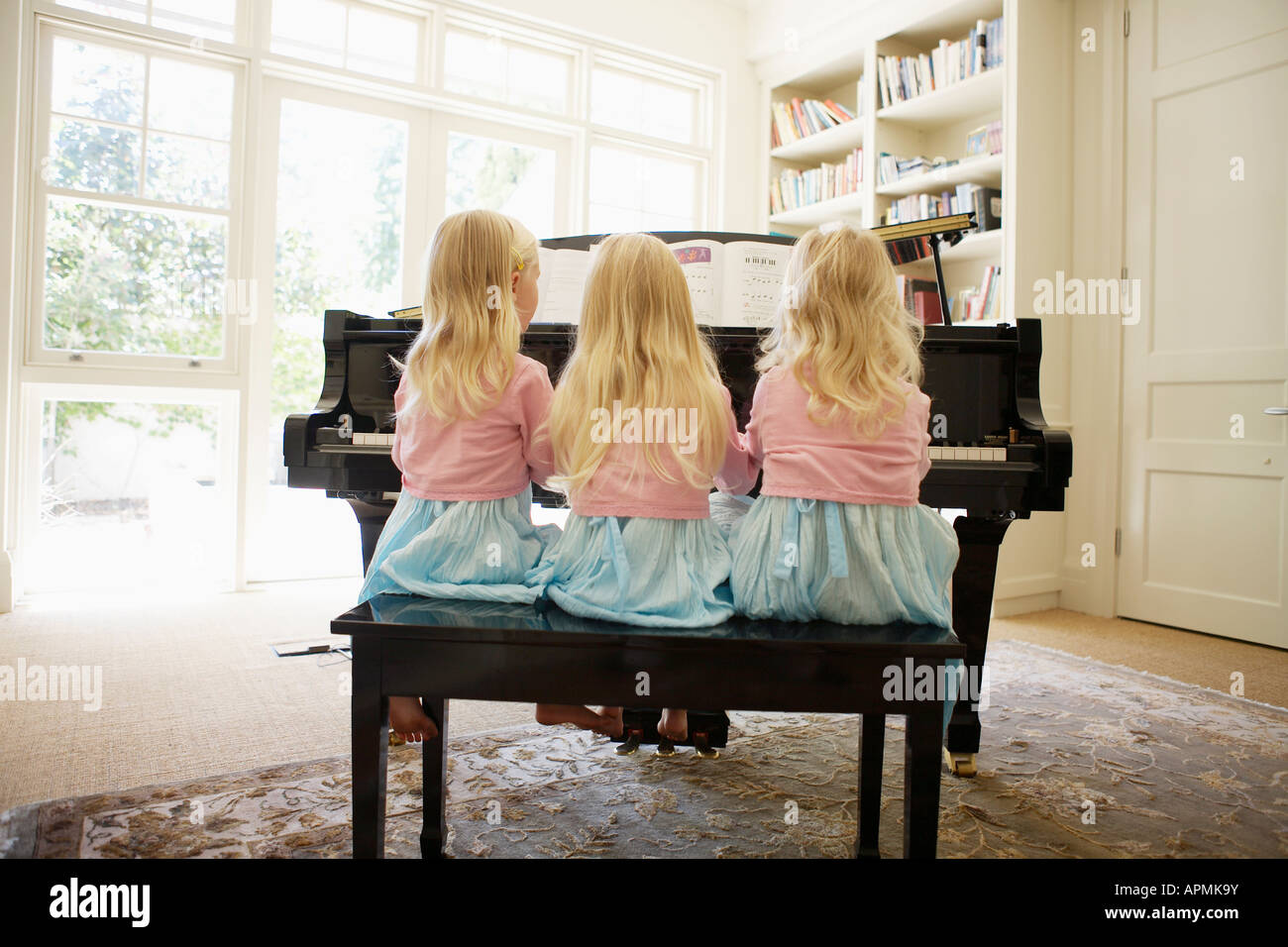 Triplets playing piano in living room (rear view Stock Photo - Alamy