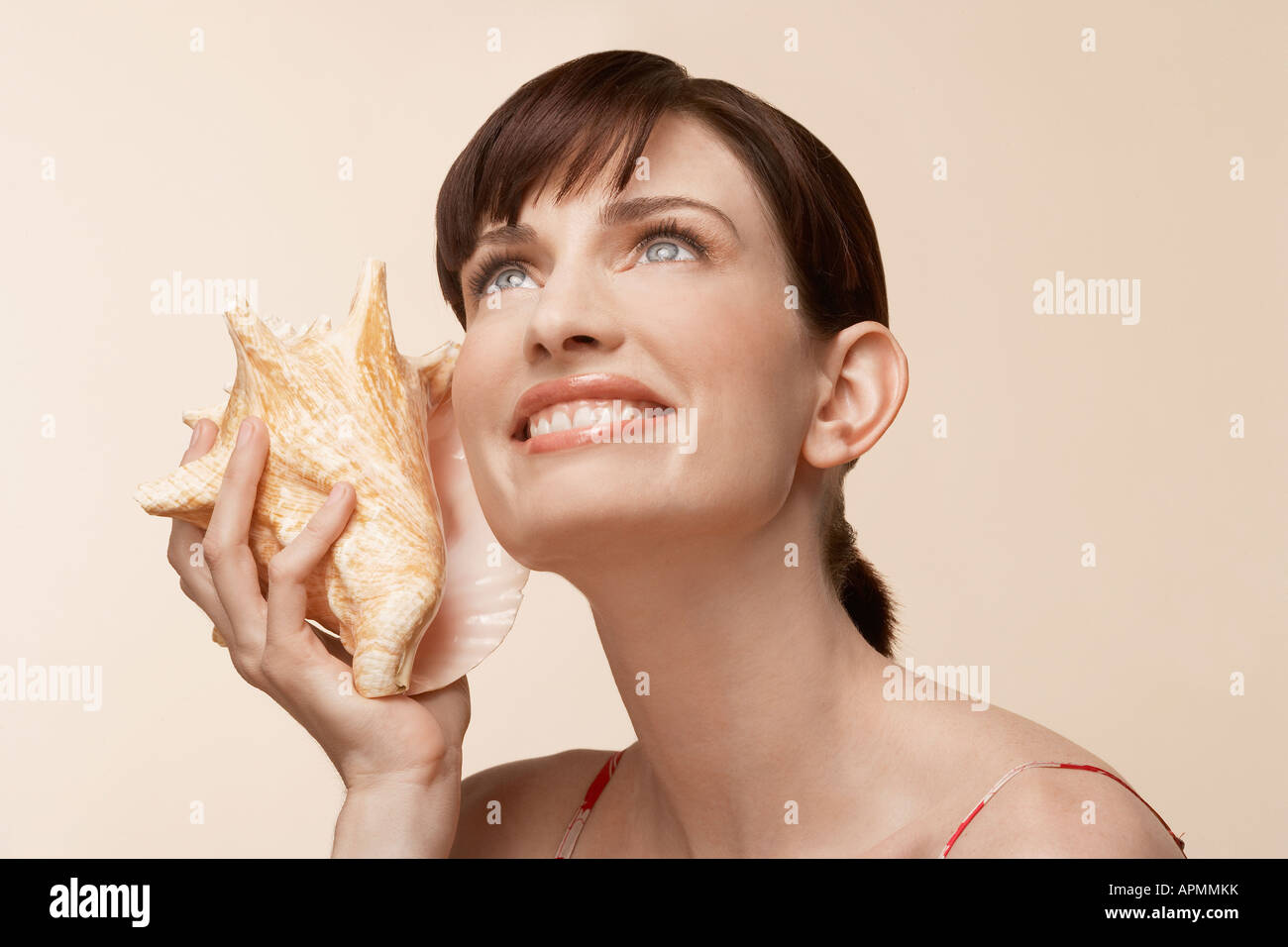 Mid adult woman holding conch shell to ear Stock Photo - Alamy