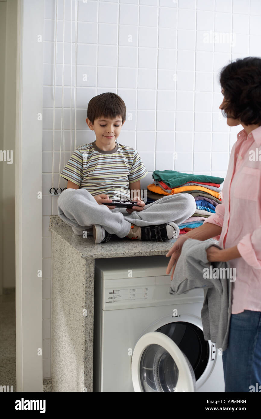 Son playing video game while mother loading washing machine Stock Photo ...