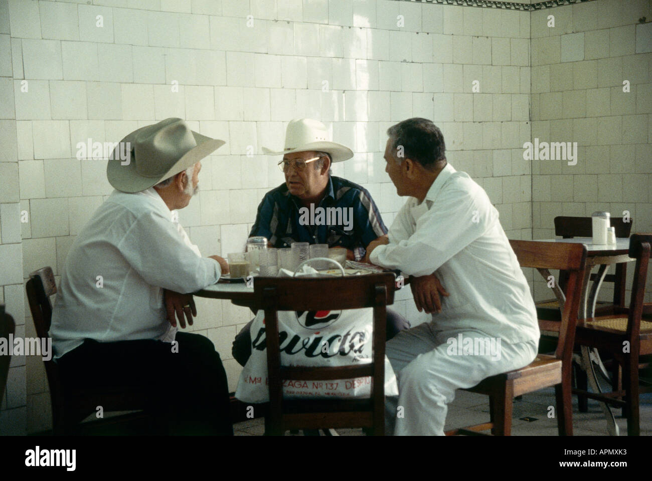 Three local men sitting chatting over a drink around a table next to a ...