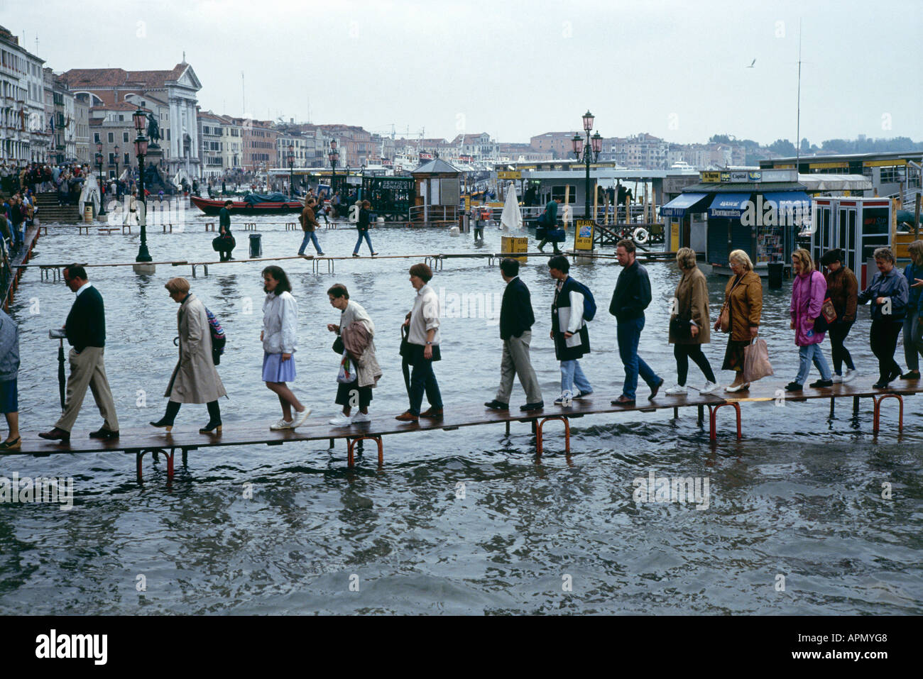 A line of people walking in single file across temporary boards set ...