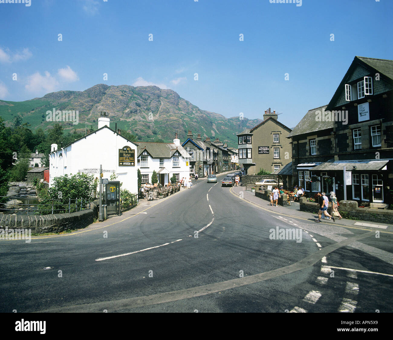 The main street in Coniston beyond trees and hills in the Lake District ...