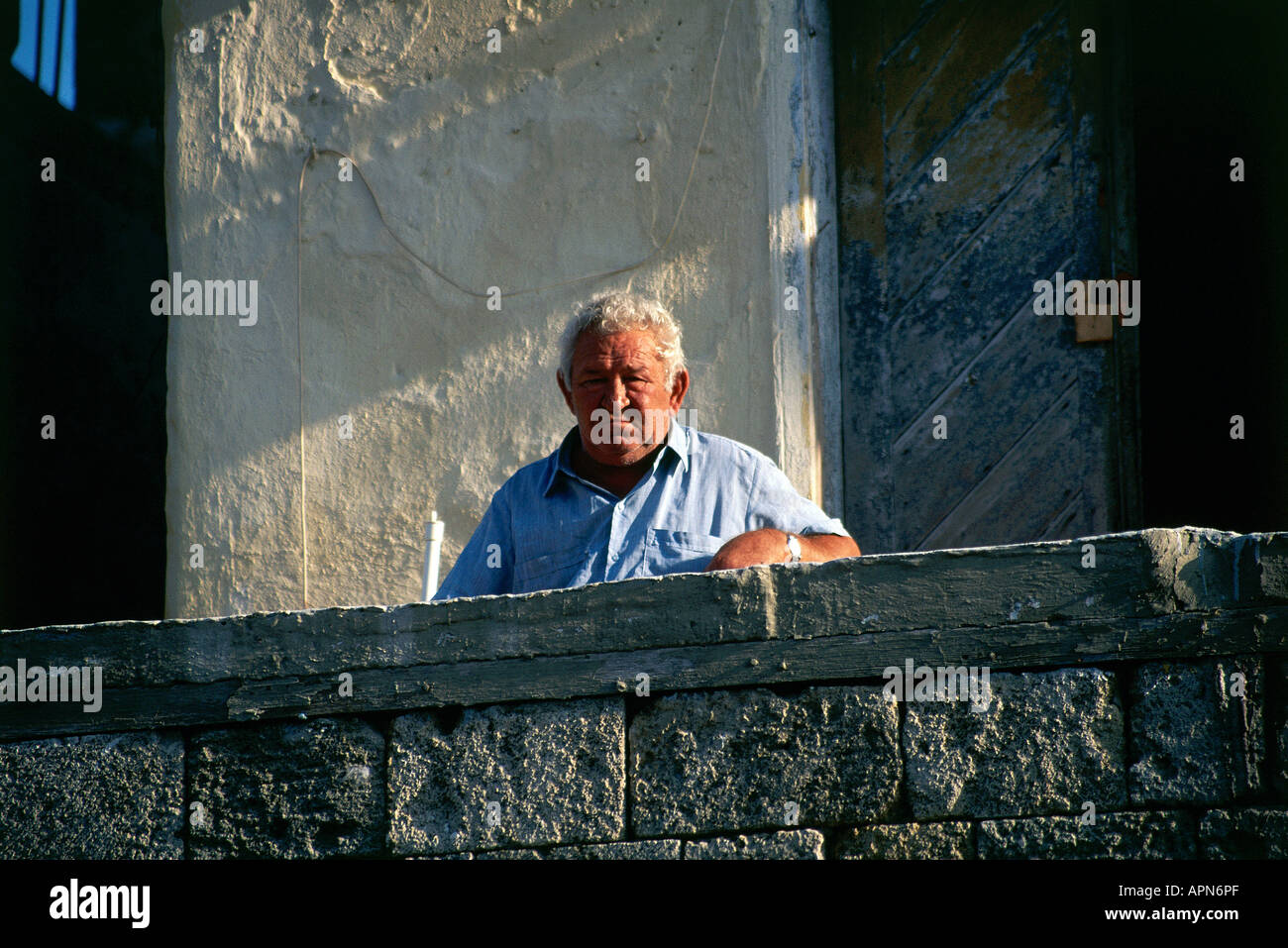 A Greek man standing in the sunshine on an upper floor balcony in Odos ...