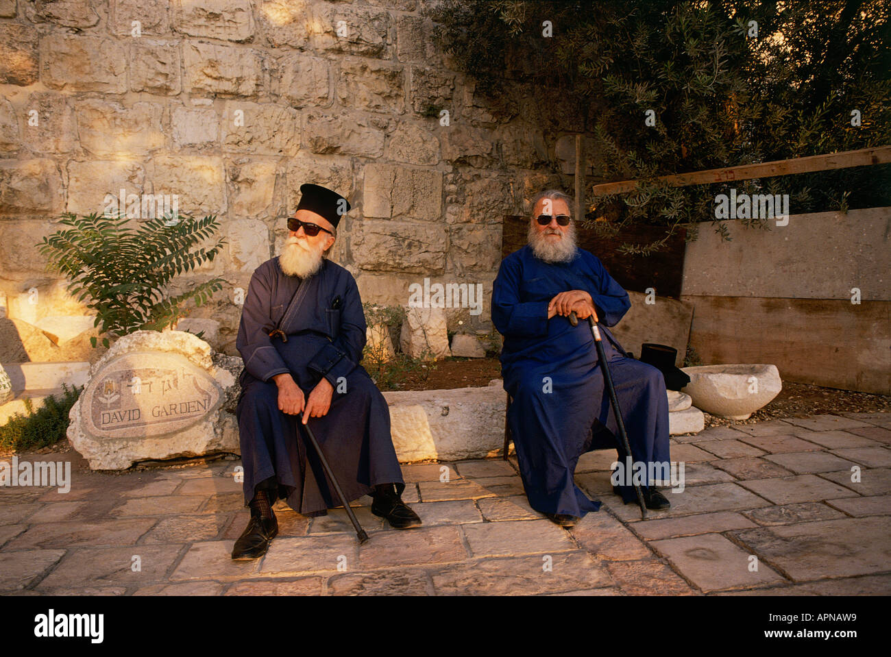 Elderly Orthodox priests seated relaxing in a secluded sunny courtyard ...