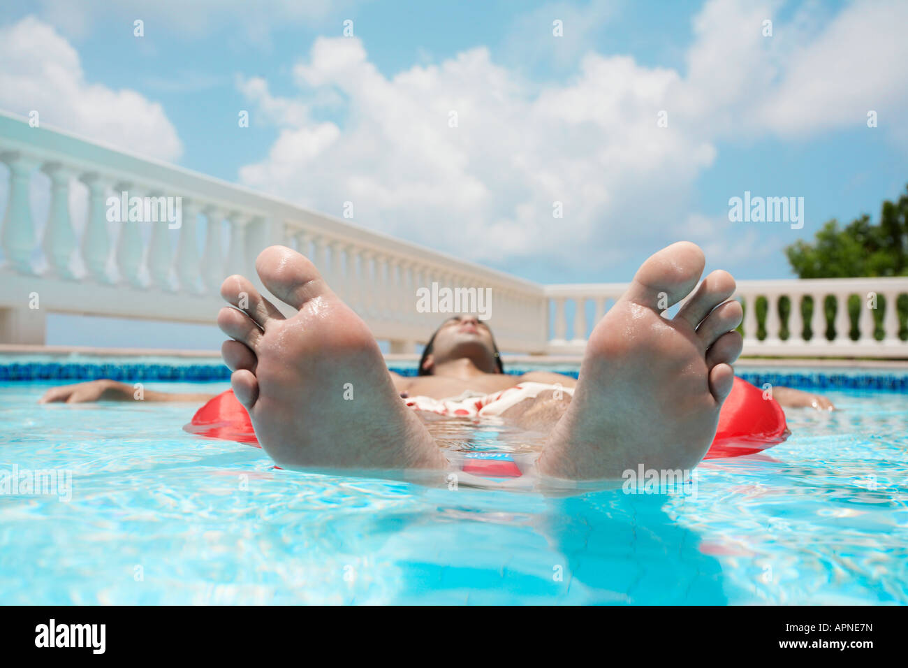 Young man lying on pool raft in swimming pool (focus on feet, surface ...