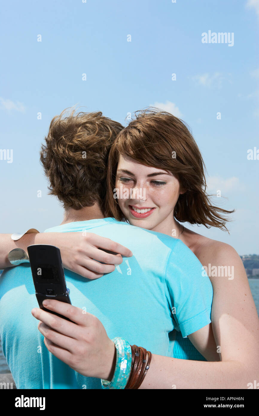 Teenage girl hugging boyfriend and using mobile phone Stock Photo - Alamy