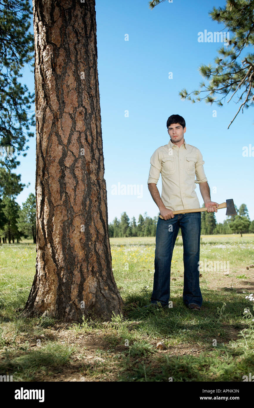 Young man with axe standing by tree Stock Photo - Alamy