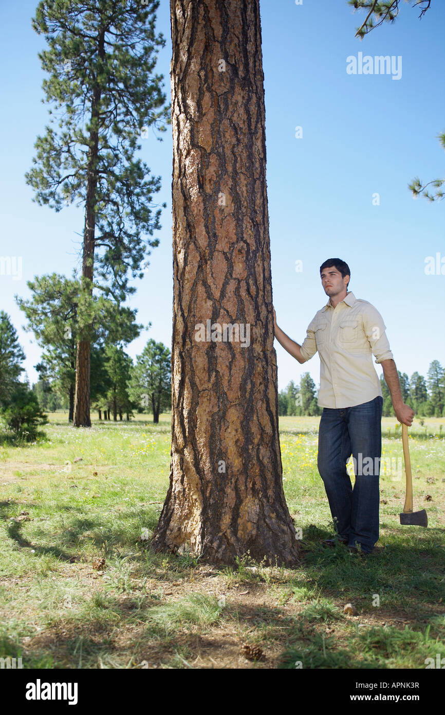 Young man with axe standing by tree Stock Photo - Alamy