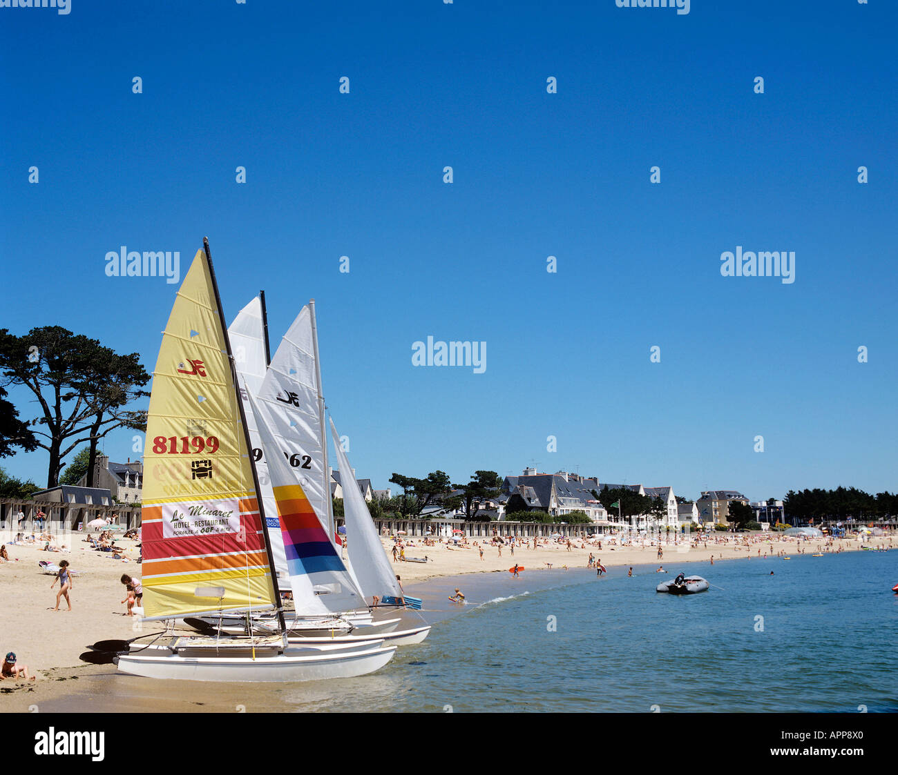 A line of small sailing dinghies drawn up in the shallows on the beach ...
