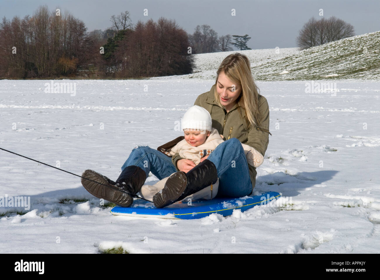 mother and one year old baby son having fun in snow on a sledge ...