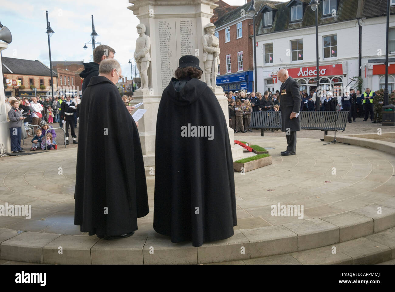 Clergy in black cloaks stand around war memorial as wreaths are laid ...