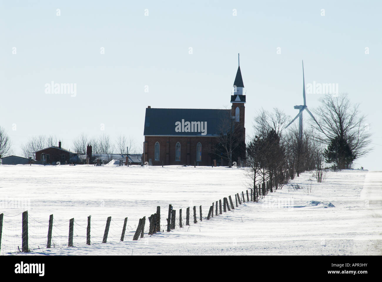 A wind turbine shows behind a church on a snowy hill Ontario Canada ...