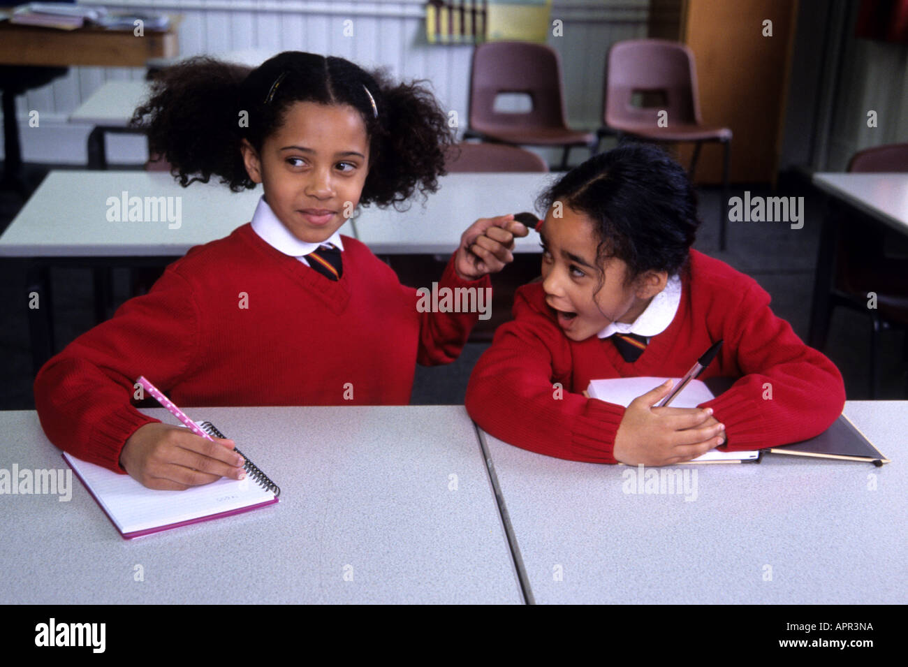 Two little black girls in a classroom. One is pulling the others hair ...
