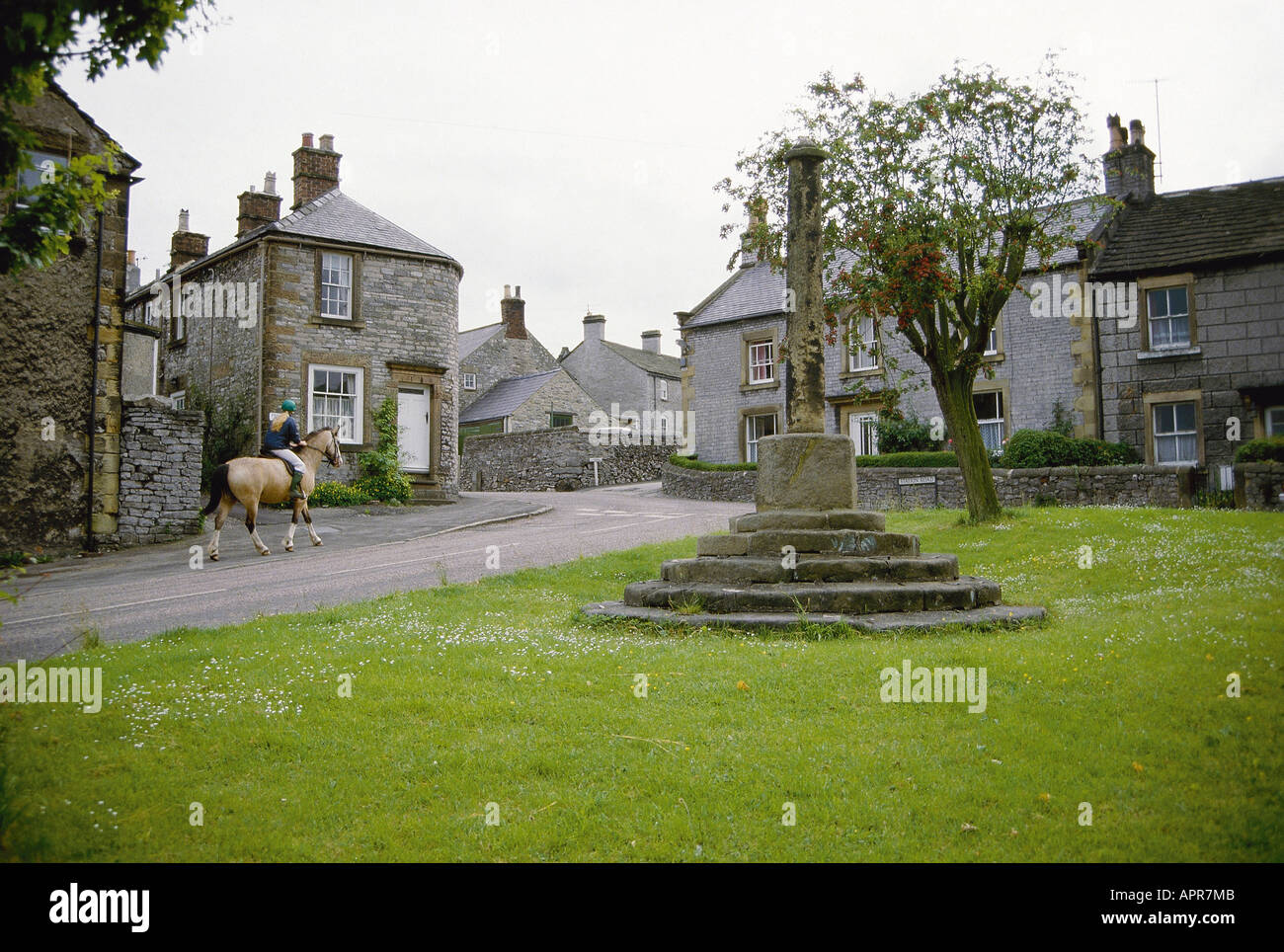 A medieval village cross stands on the small green in the limestone ...