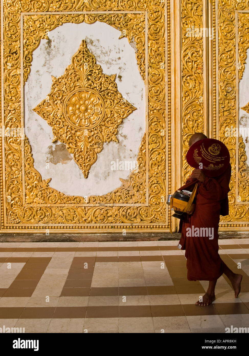 A monk collecting alms shields his face from the sun at Shwedagon Paya ...