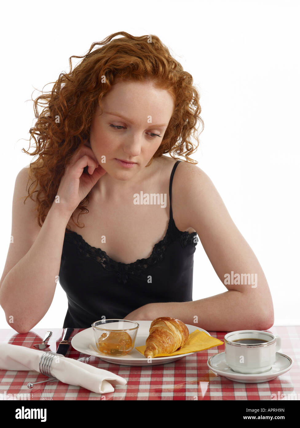 Young woman sitting at breakfast table croissant with marmalade cup of ...