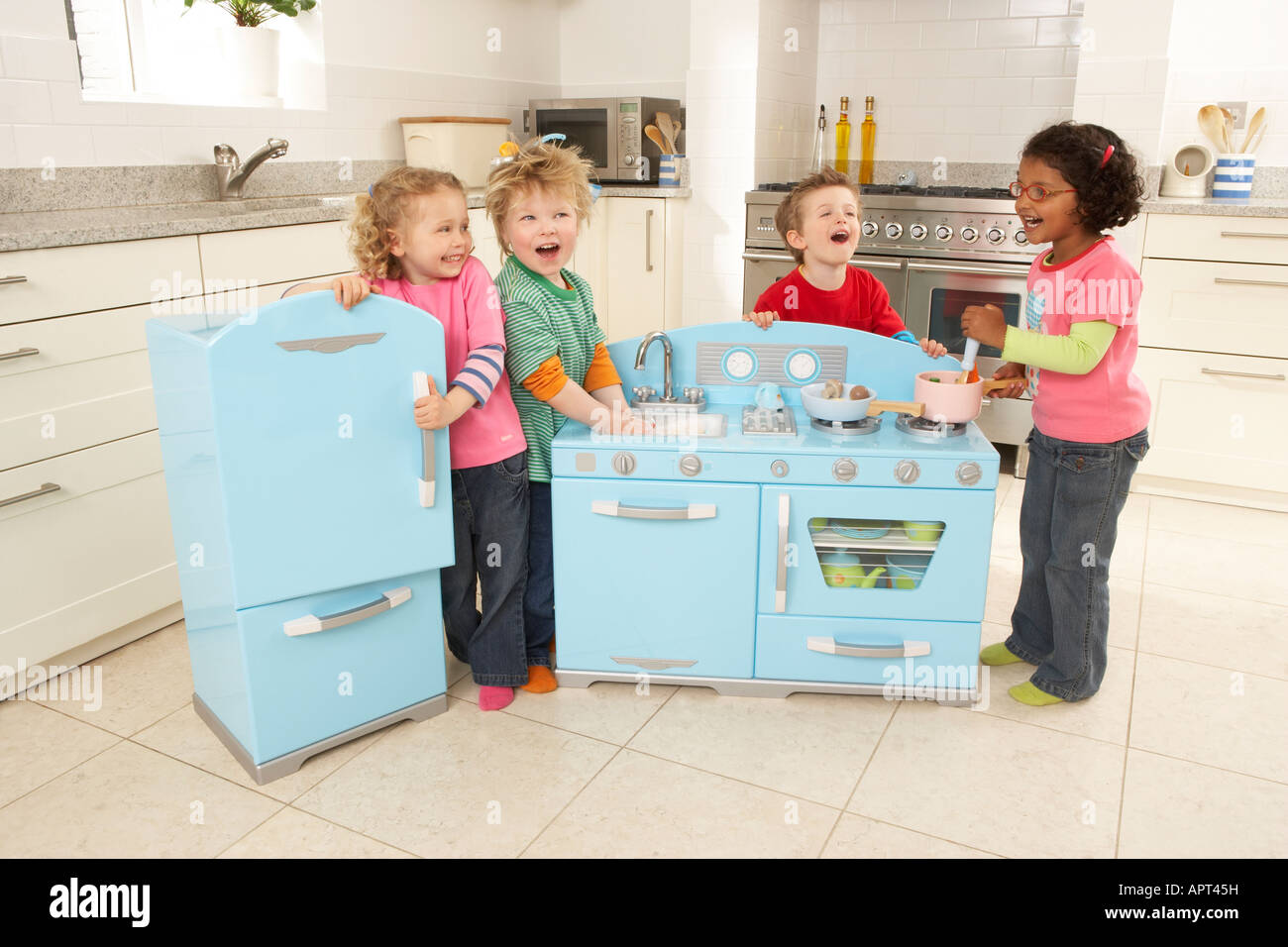 four children laugh as they play in a kitchen with a toy kitchen set ...
