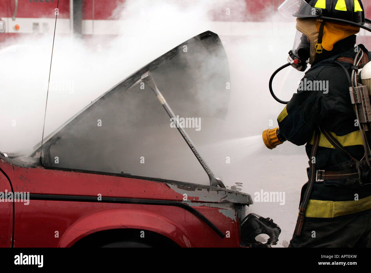 A firefighter using a hoseline to extinguish a car fire while pointing ...