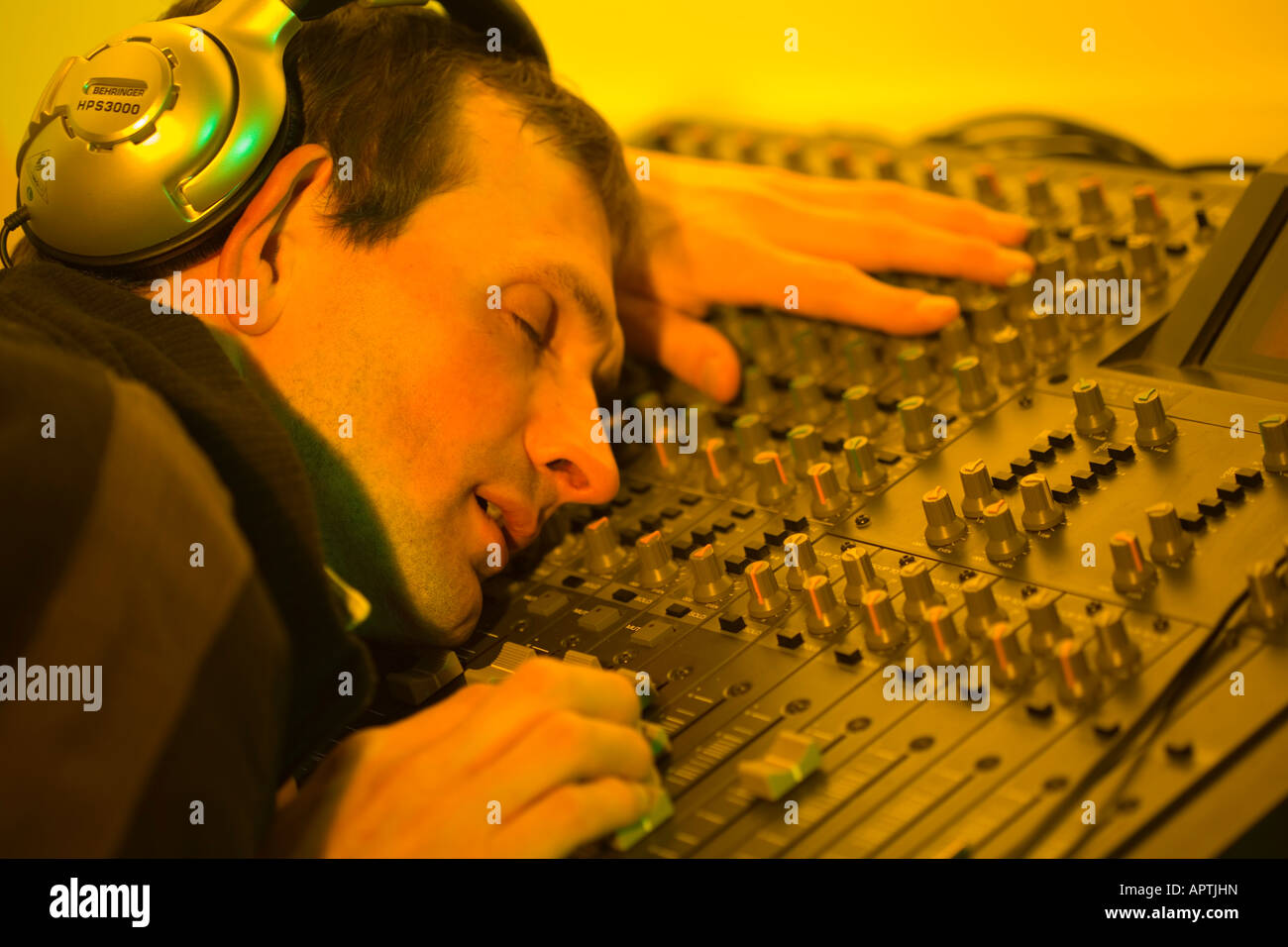 Man slumped across mixing desk with eyes shut and headphones falling ...