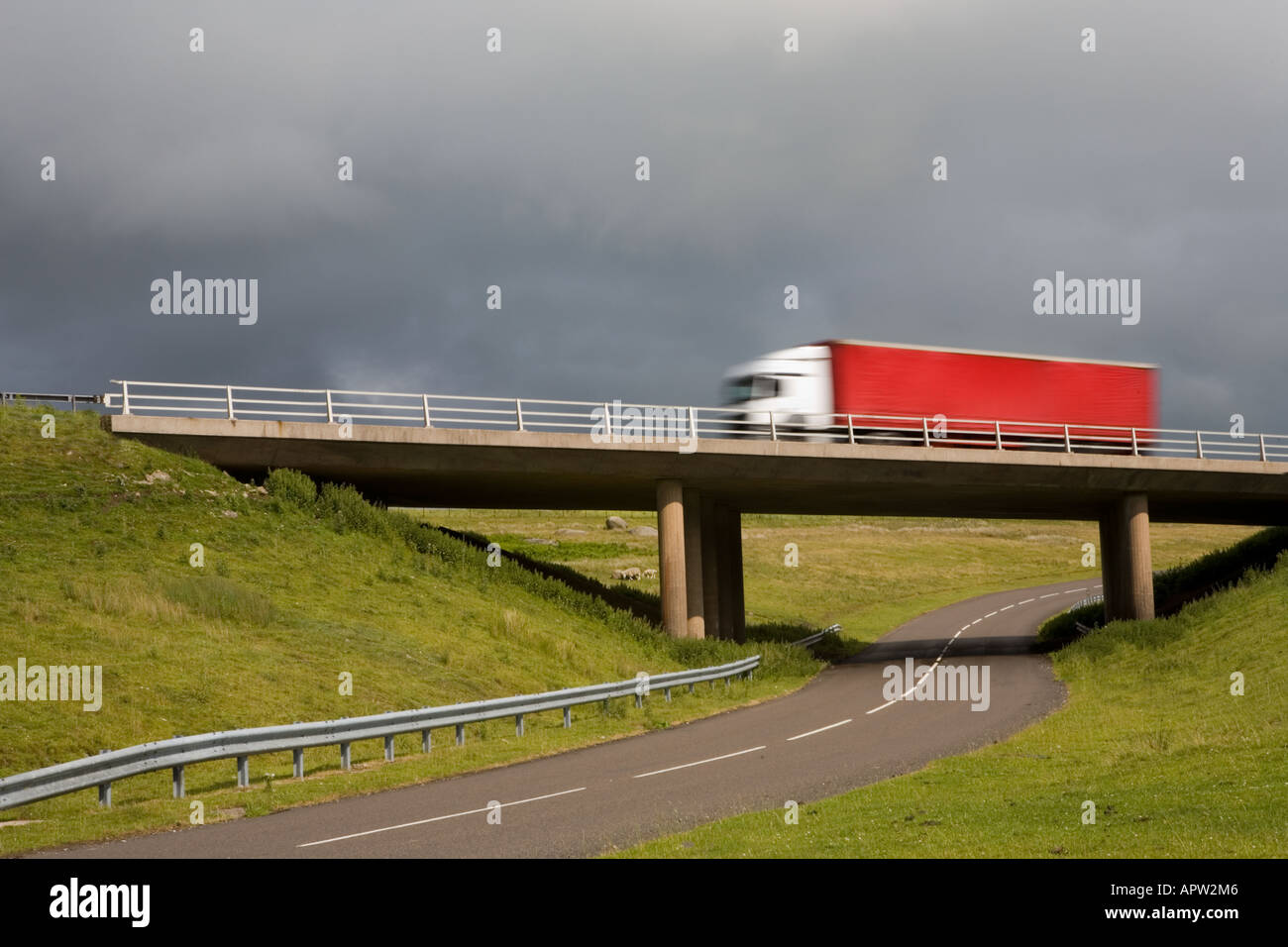 Moving red lorry on motorway bridge over a road with grass banks on ...