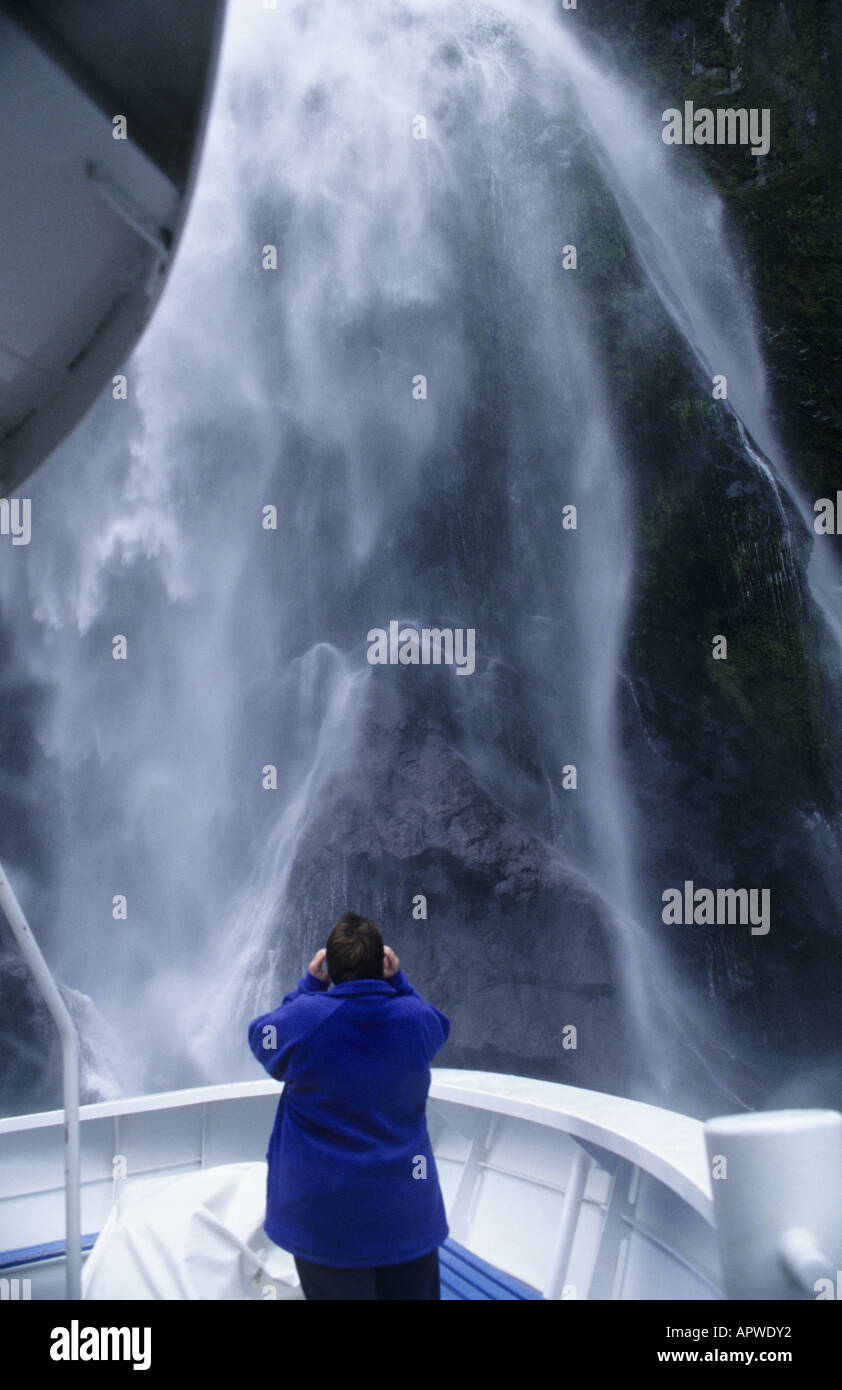 A tourist on the stern of a cruise ship taking pictures of a waterfall ...