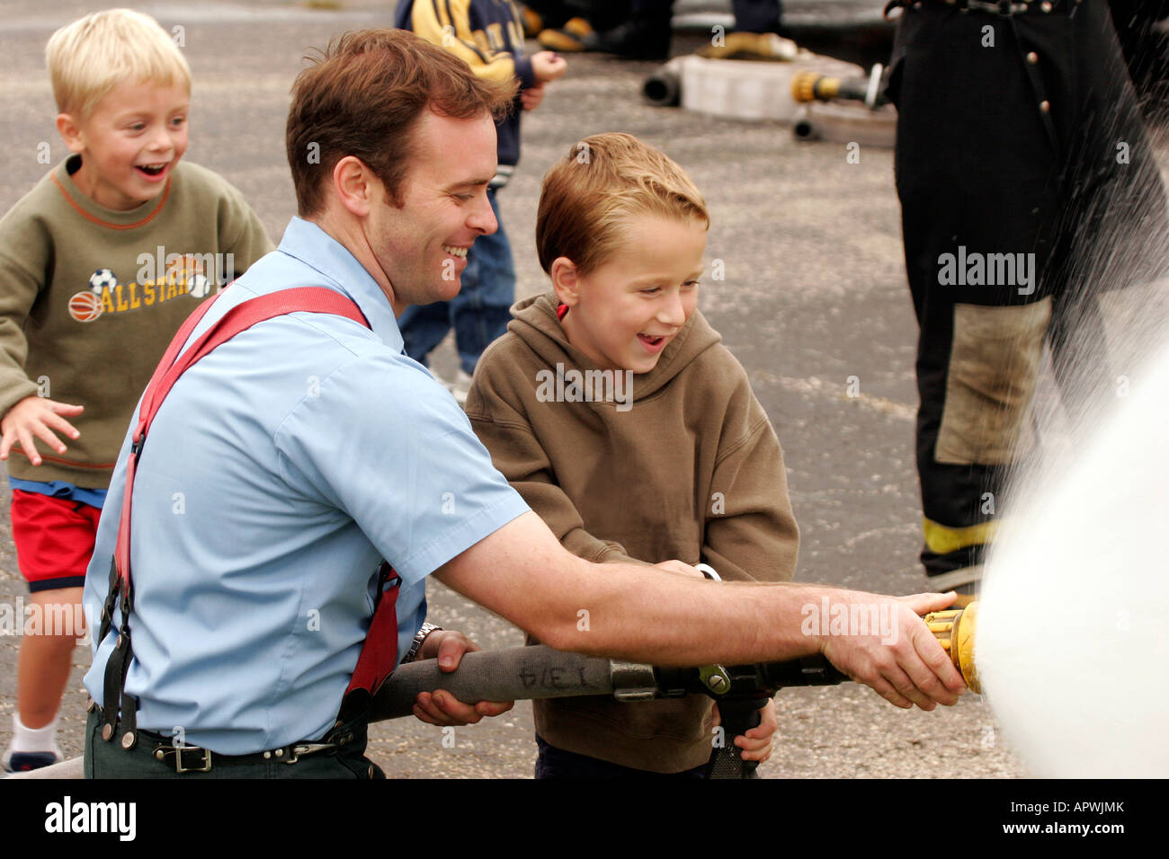 Two children getting to use a fire hose with the help of a fire fighter ...