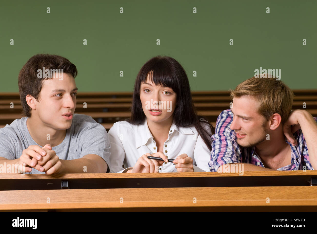 three young students sitting in lecture hall having a conversation ...