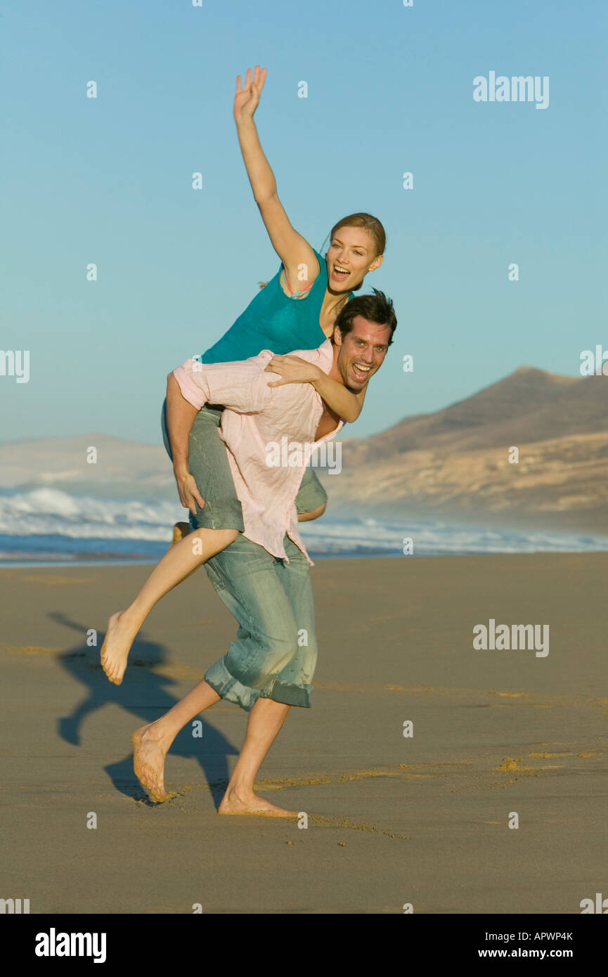 young man giving woman piggyback ride on beach Stock Photo - Alamy